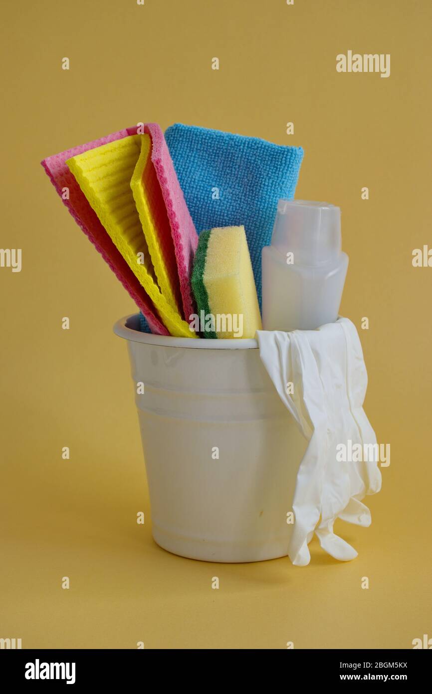 Container with cleaning items against yellow background Stock Photo - Alamy