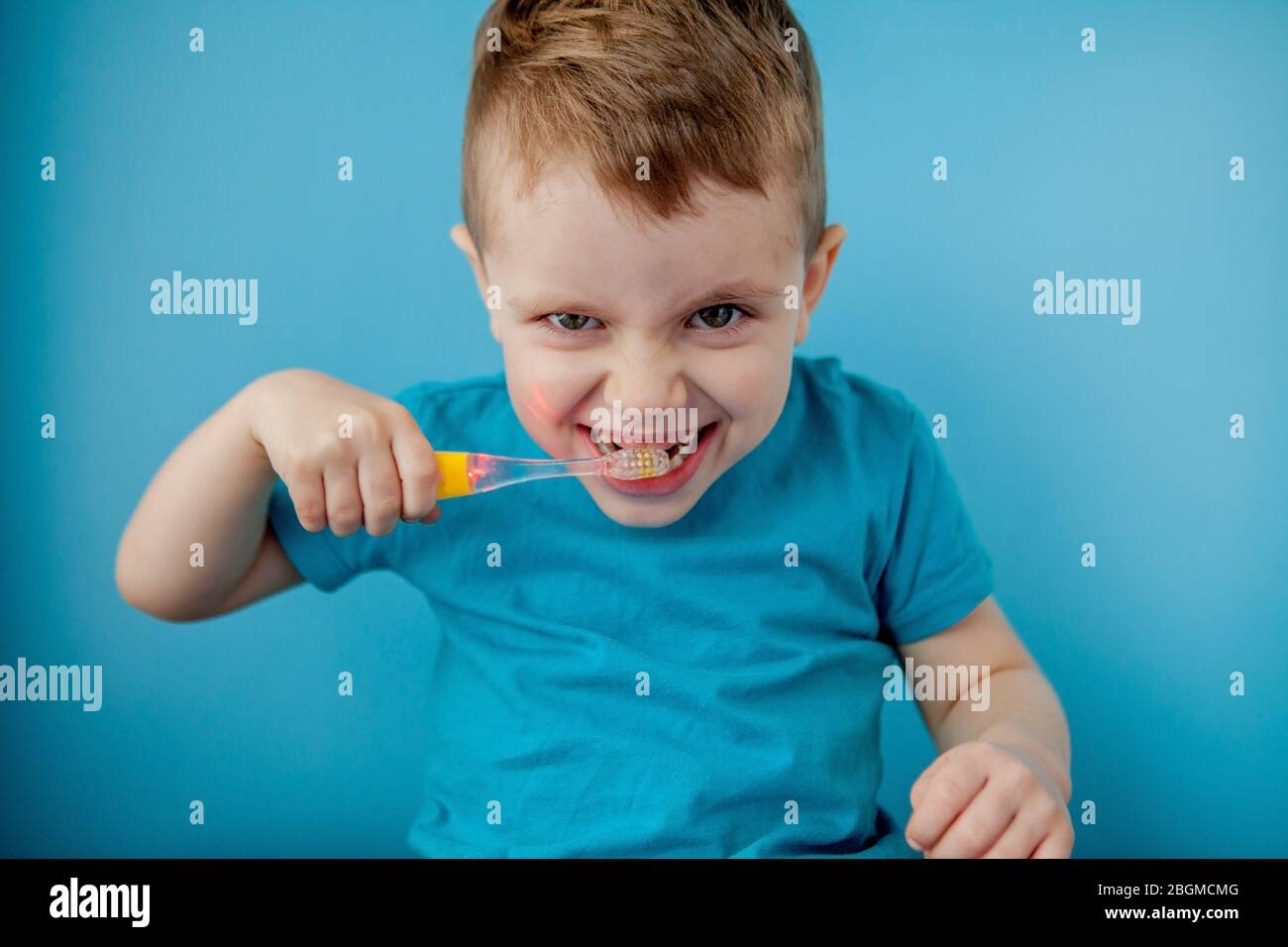 Little cute boy brushing his teeth on blue background Stock Photo - Alamy
