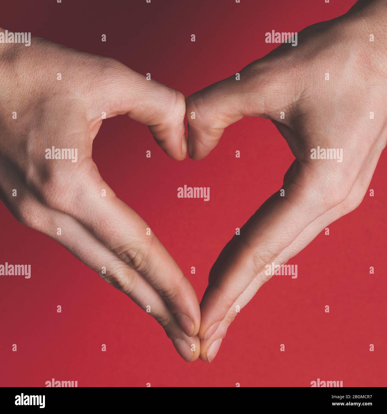 Female hands creating the shape of a love heart over a red background ...