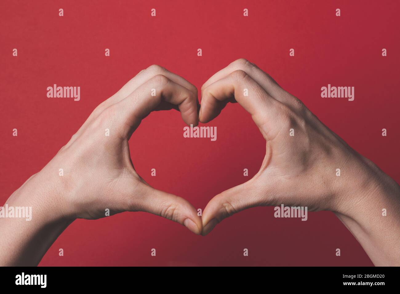 Female hands creating the shape of a love heart over a red background ...
