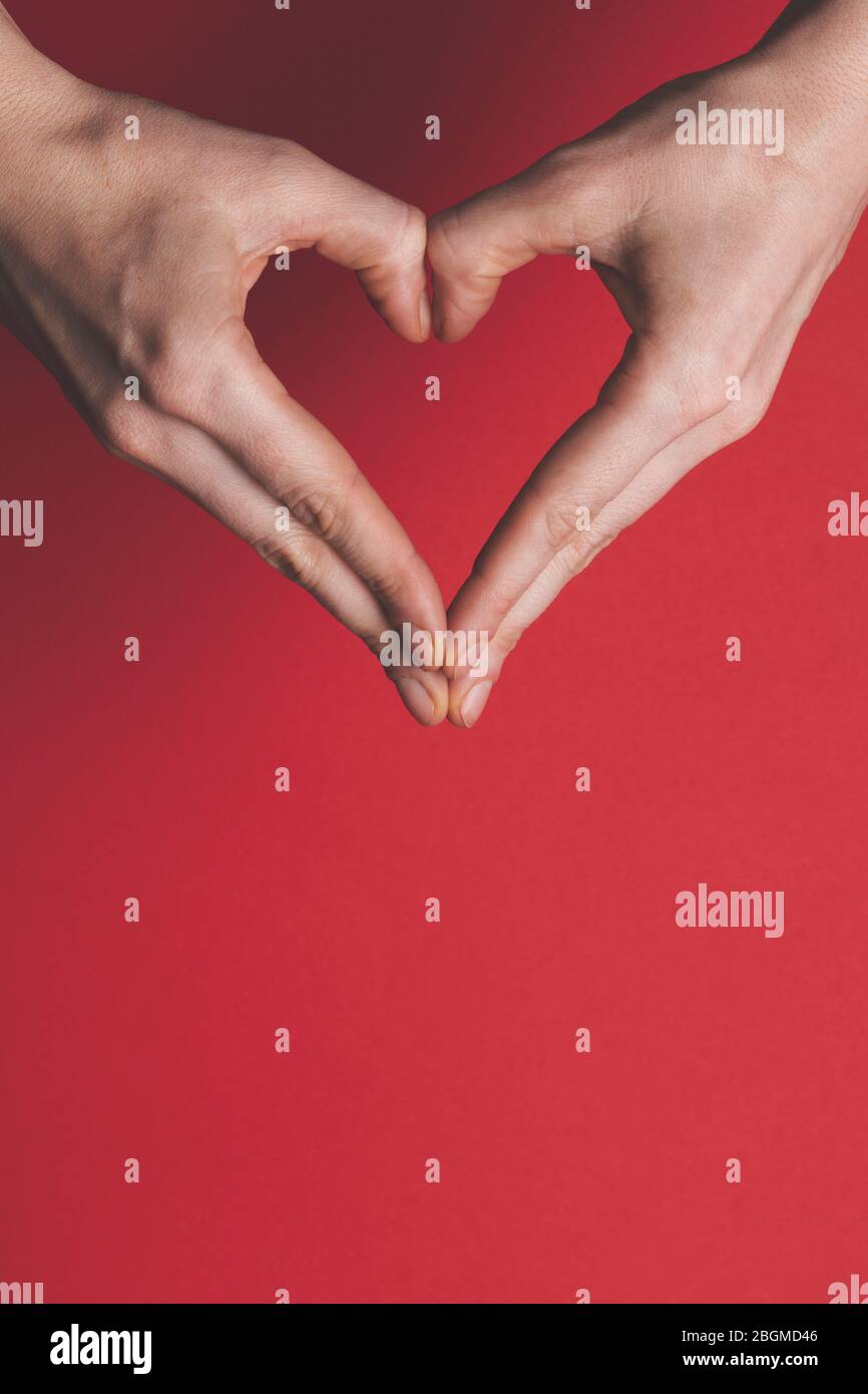 Female hands creating the shape of a love heart over a red background ...