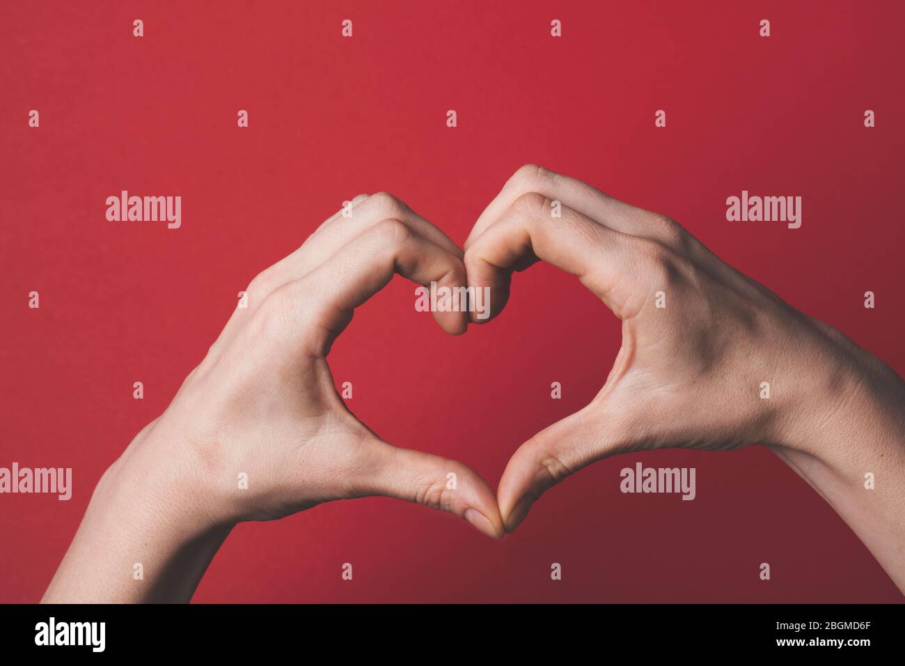Female hands creating the shape of a love heart over a red background ...