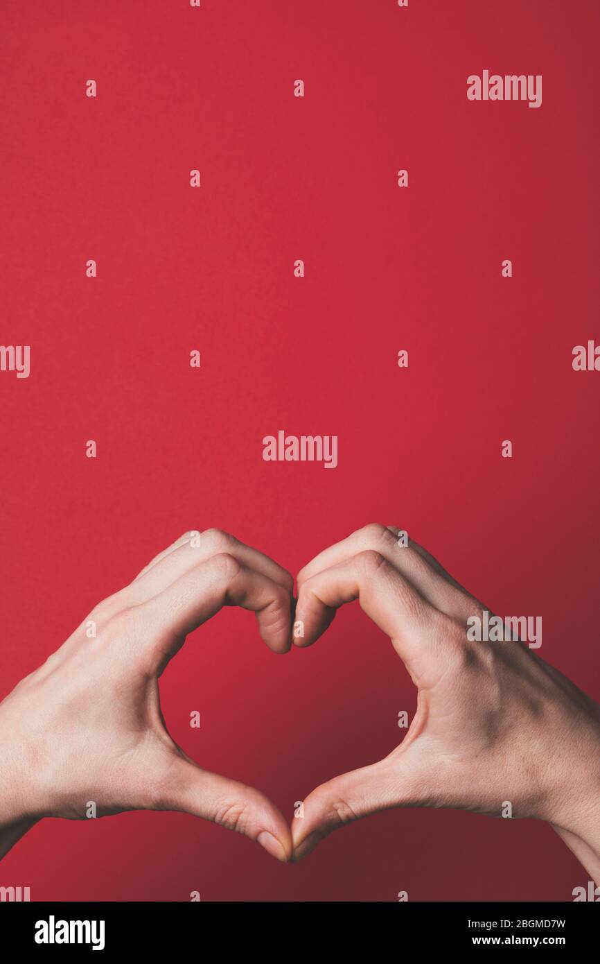 Female hands creating the shape of a love heart over a red background ...
