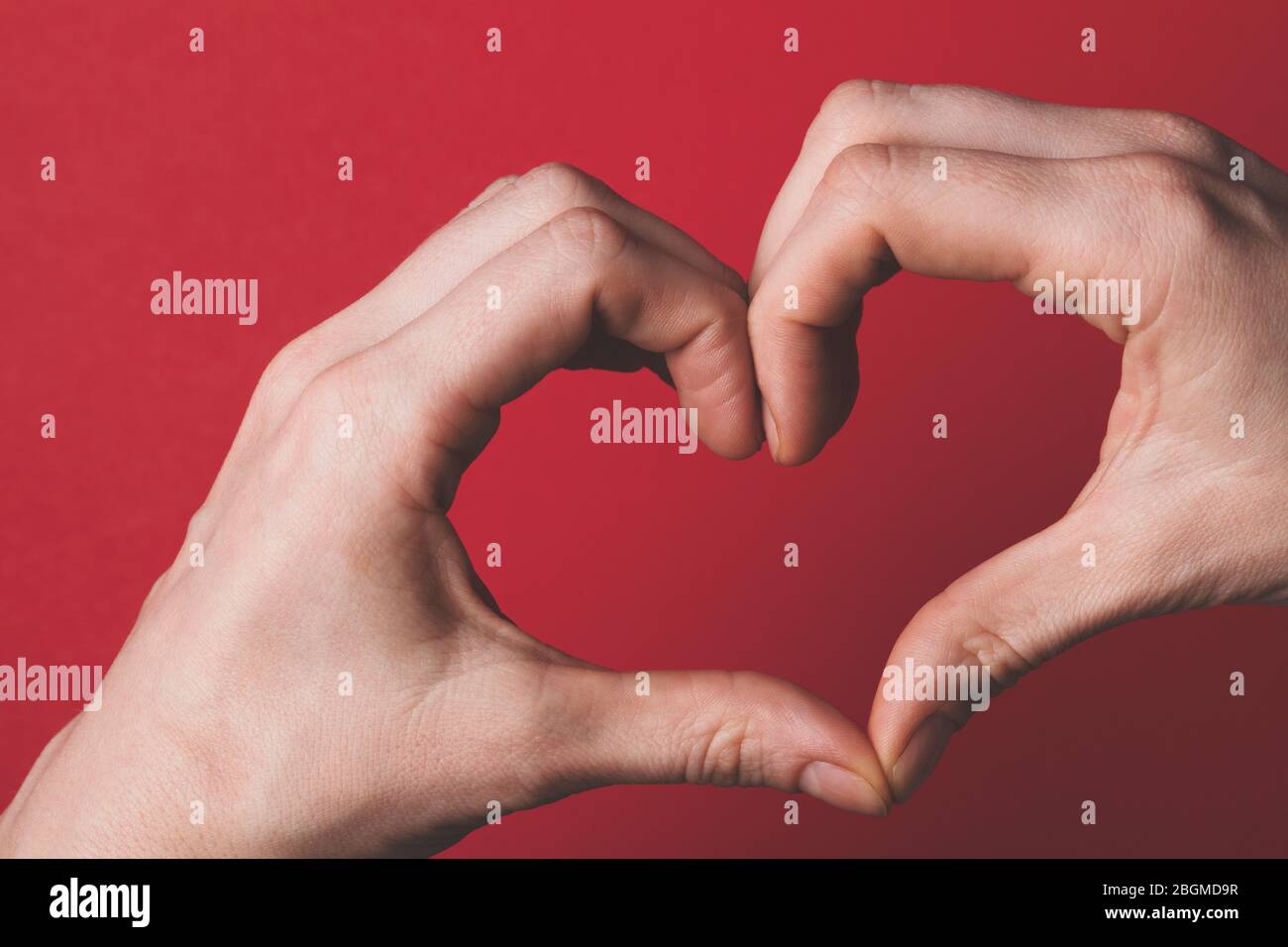 Female hands creating the shape of a love heart over a red background ...