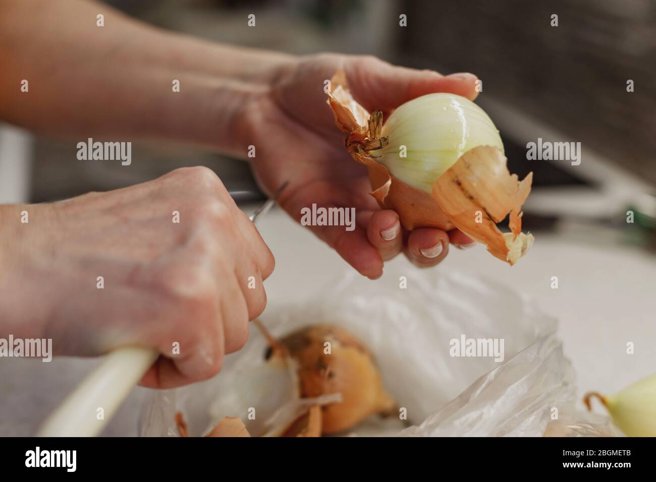 Woman's hands in process of peeling fresh onion above small plastic bag ...