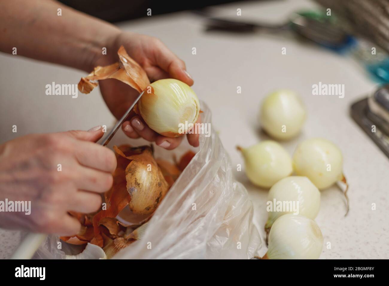 Woman's hands in process of peeling fresh onion above small plastic bag ...