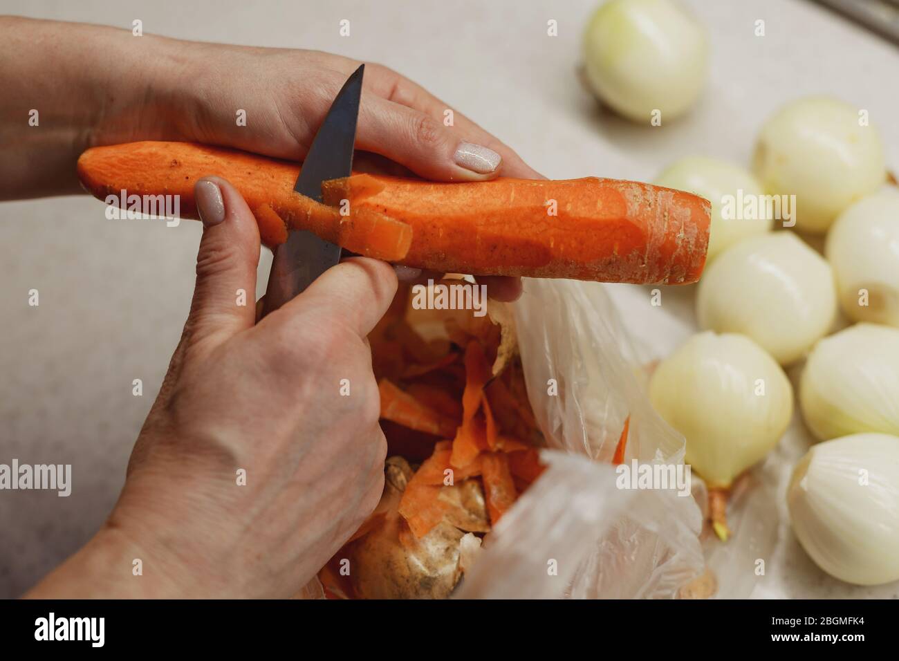 Woman's hands in process of peeling fresh carrot above small plastic ...