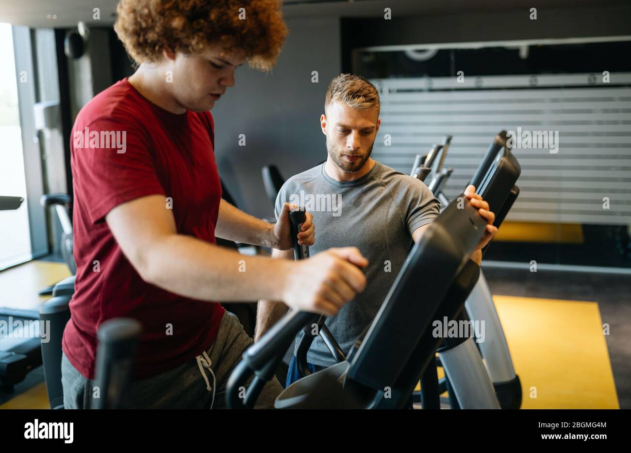 Overweight young man exercising gym with personal trainer Stock Photo ...