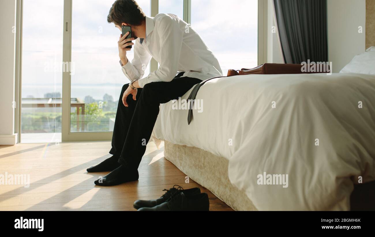 businessman sitting on his bed and talking on mobile phone. Man making ...
