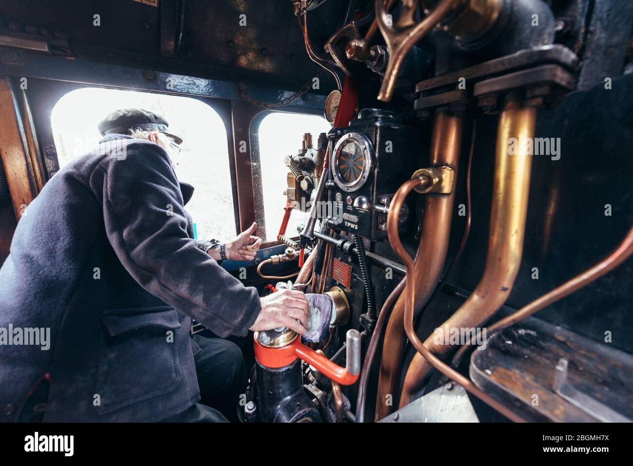 A man drives the locomotive from the cab, with his hand on a large red ...