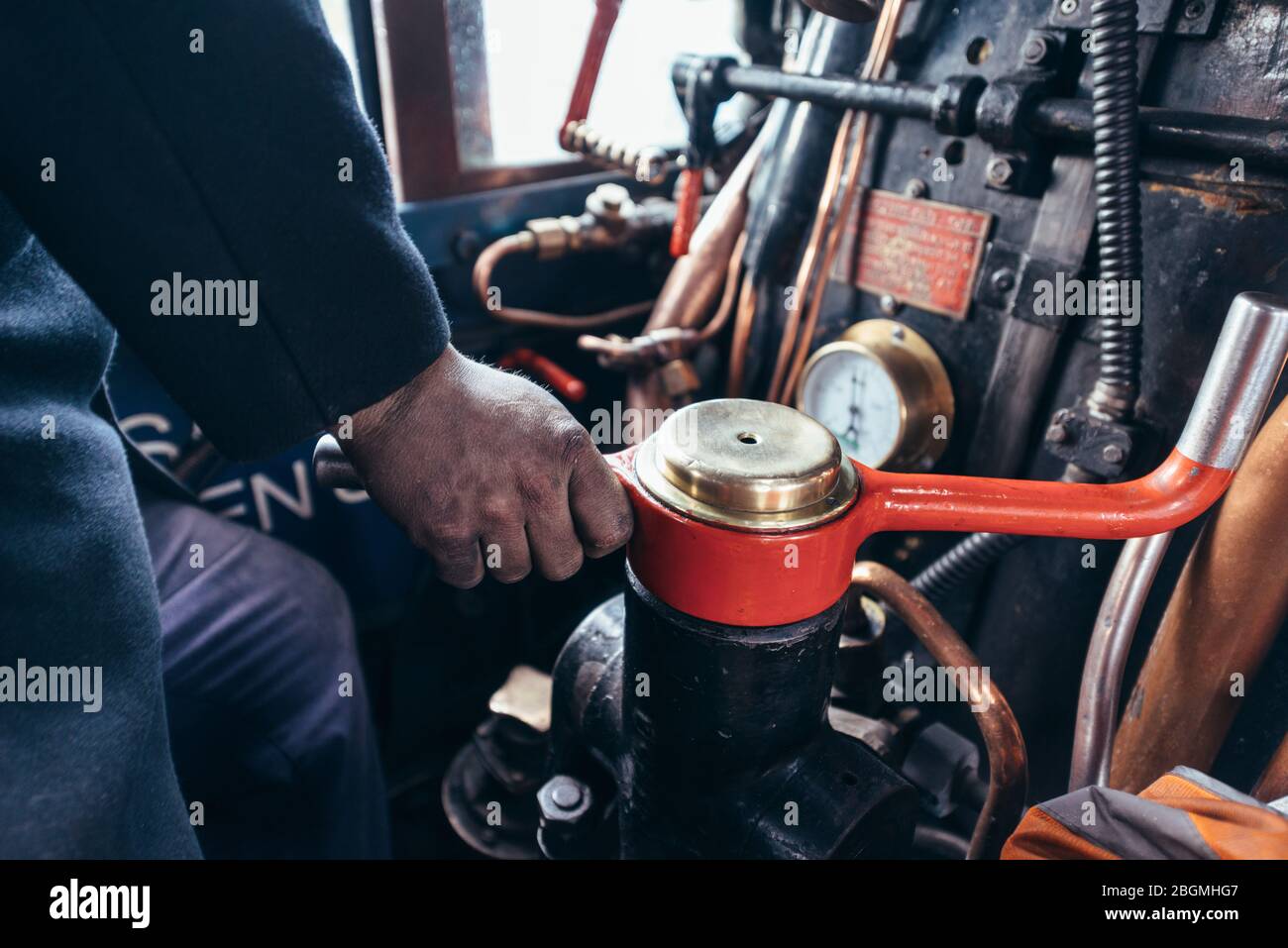 A man drives the locomotive from the cab, with his hand on a large red ...