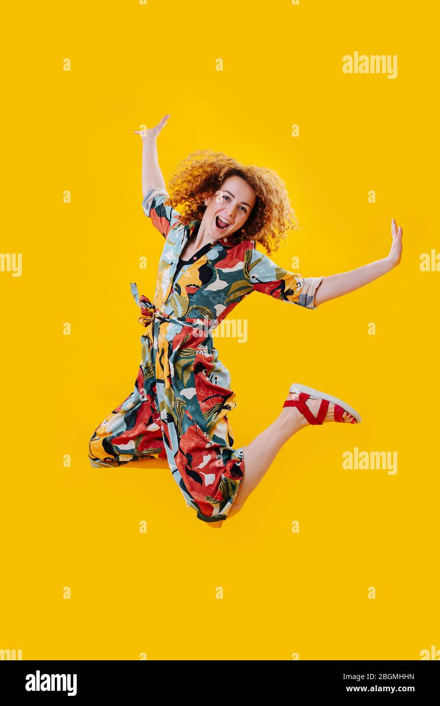 Cheerful exhilarated woman jumping in the air over yellow Stock Photo ...
