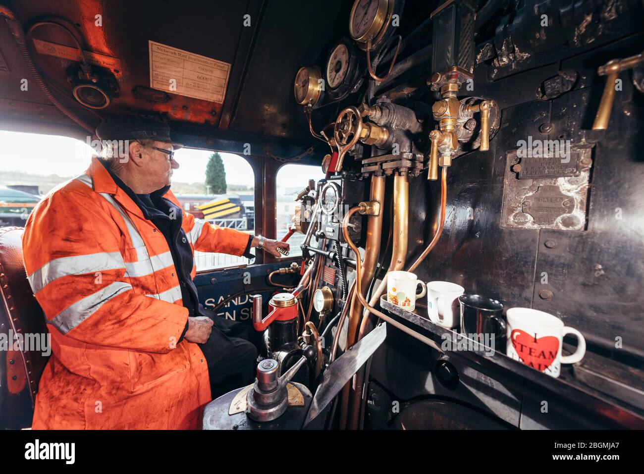 A man looks out of the cab whilst driving the locomtive, holding a ...