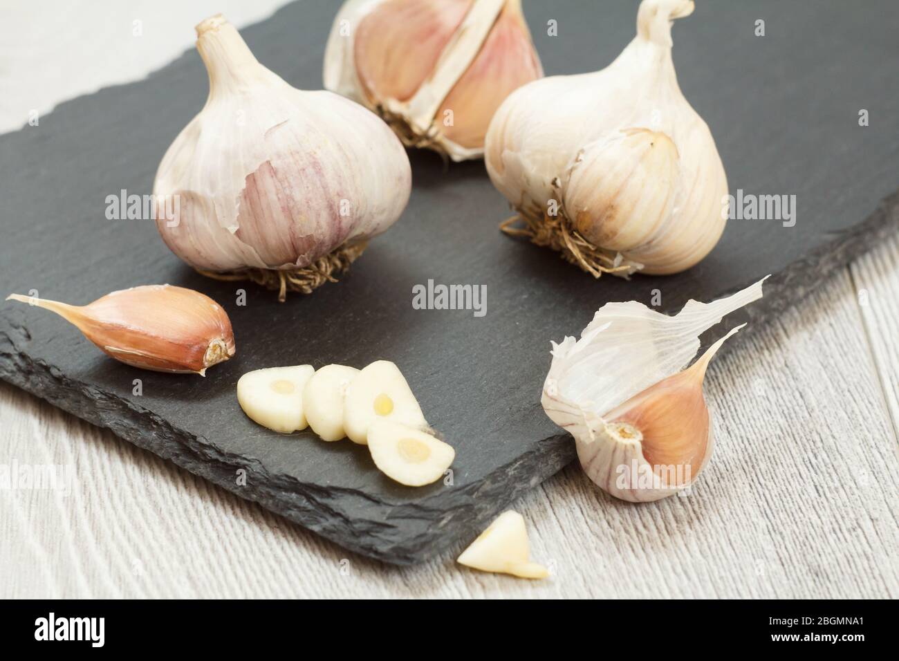 Close-up view of raw peeled and unpeeled garlic bulbs on a black stone ...