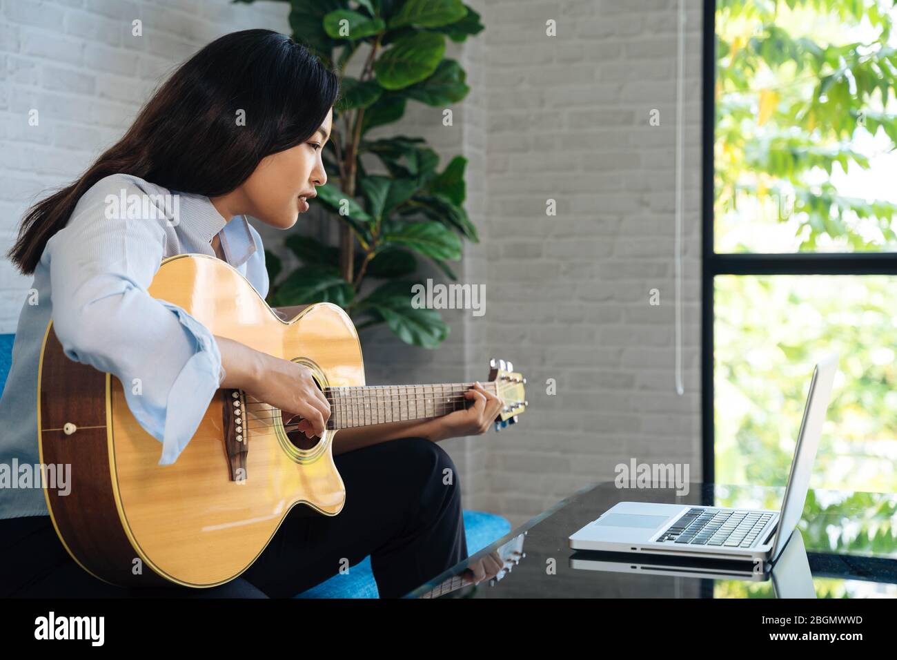 Young Asian woman practicing and learning how to play guitar on laptop ...