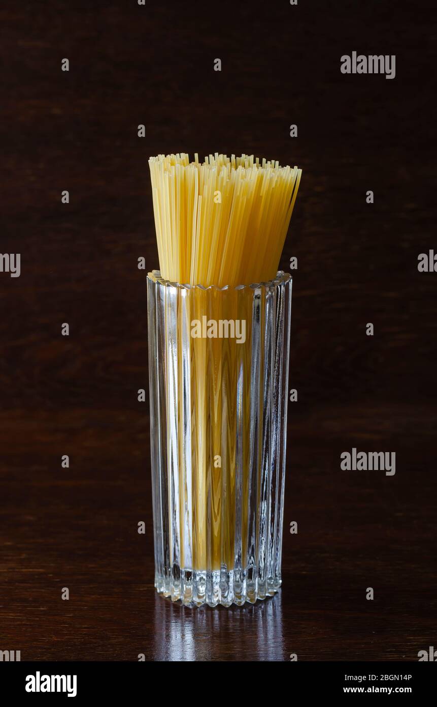 Spaghetti in a glass cup on a brown wooden table. A bunch of spaghetti ...