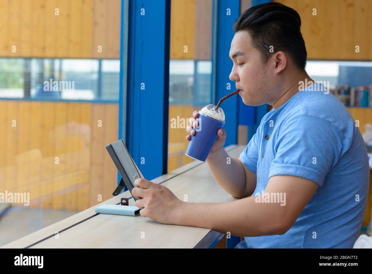 Young overweight Asian man reading book while drinking coffee Stock ...