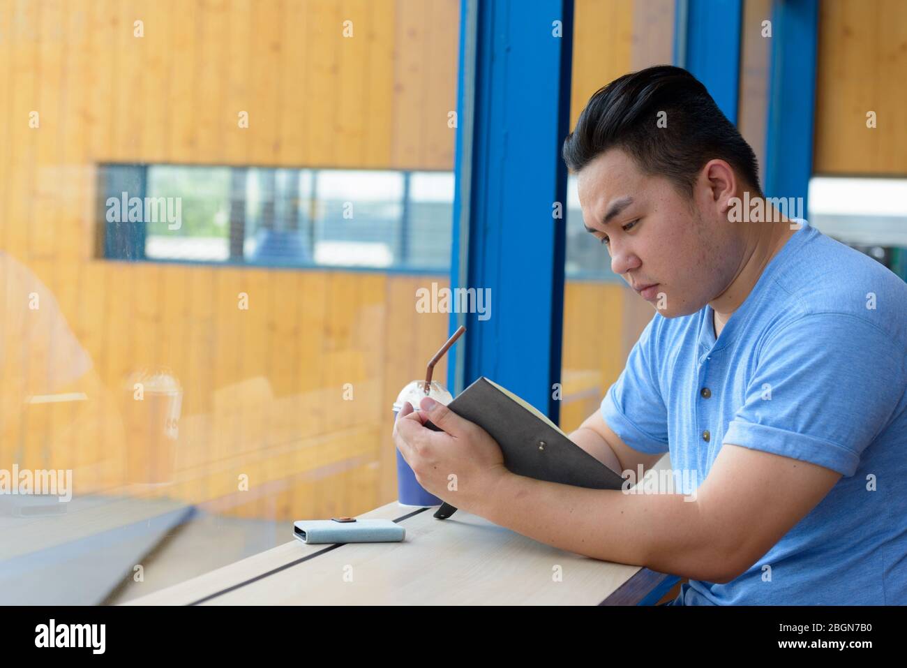 Young overweight Asian man reading book at the coffee shop Stock Photo ...