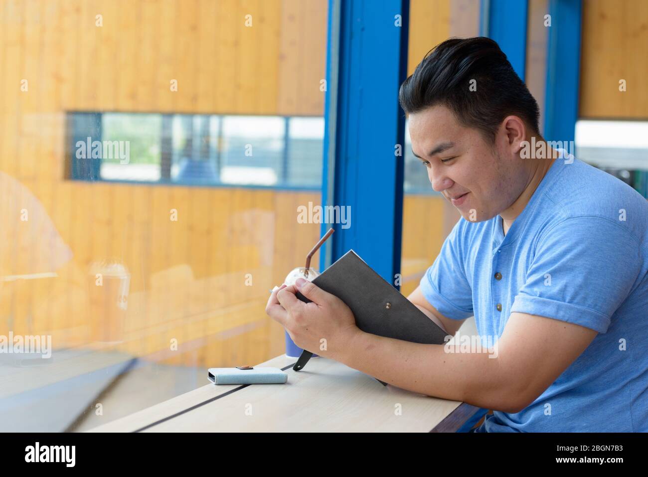 Happy young overweight Asian man reading book at the coffee shop Stock ...