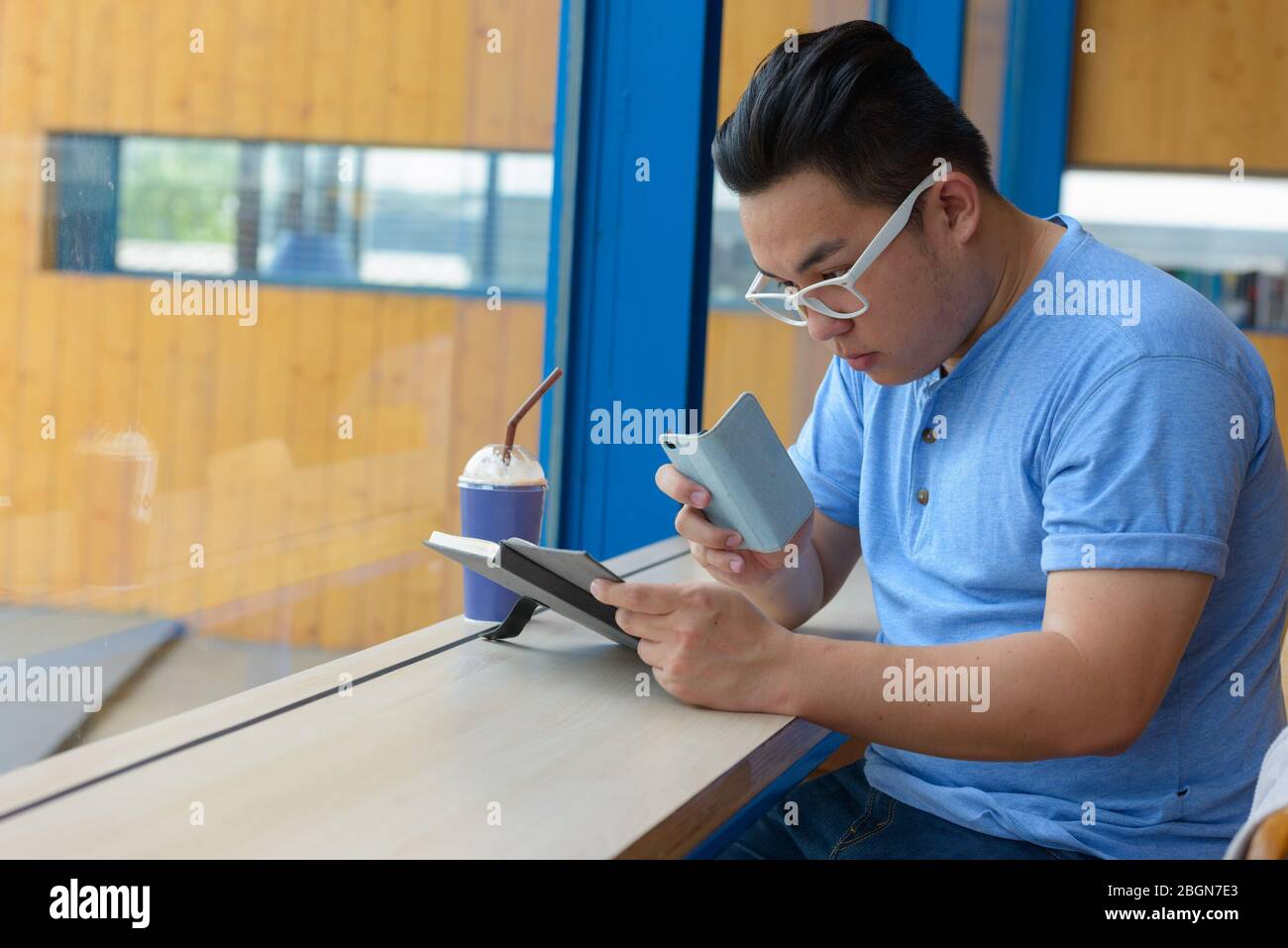 Young overweight Asian nerd man taking picture with book at the coffee ...