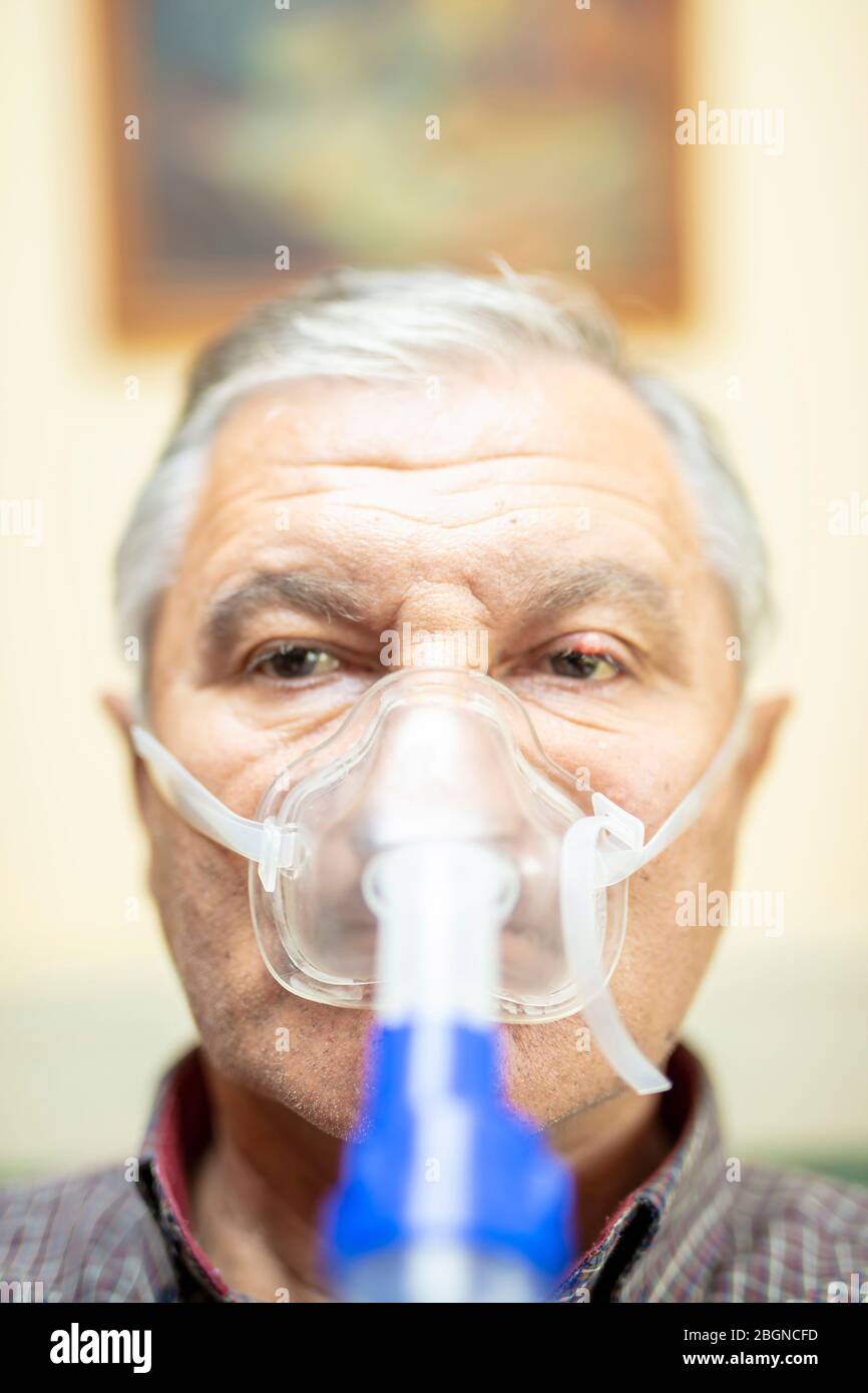 Senior man using medical equipment for inhalation with respiratory mask ...