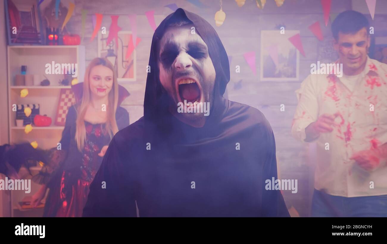 Zoom in shot of grim reaper screaming at halloween party . Group of ...