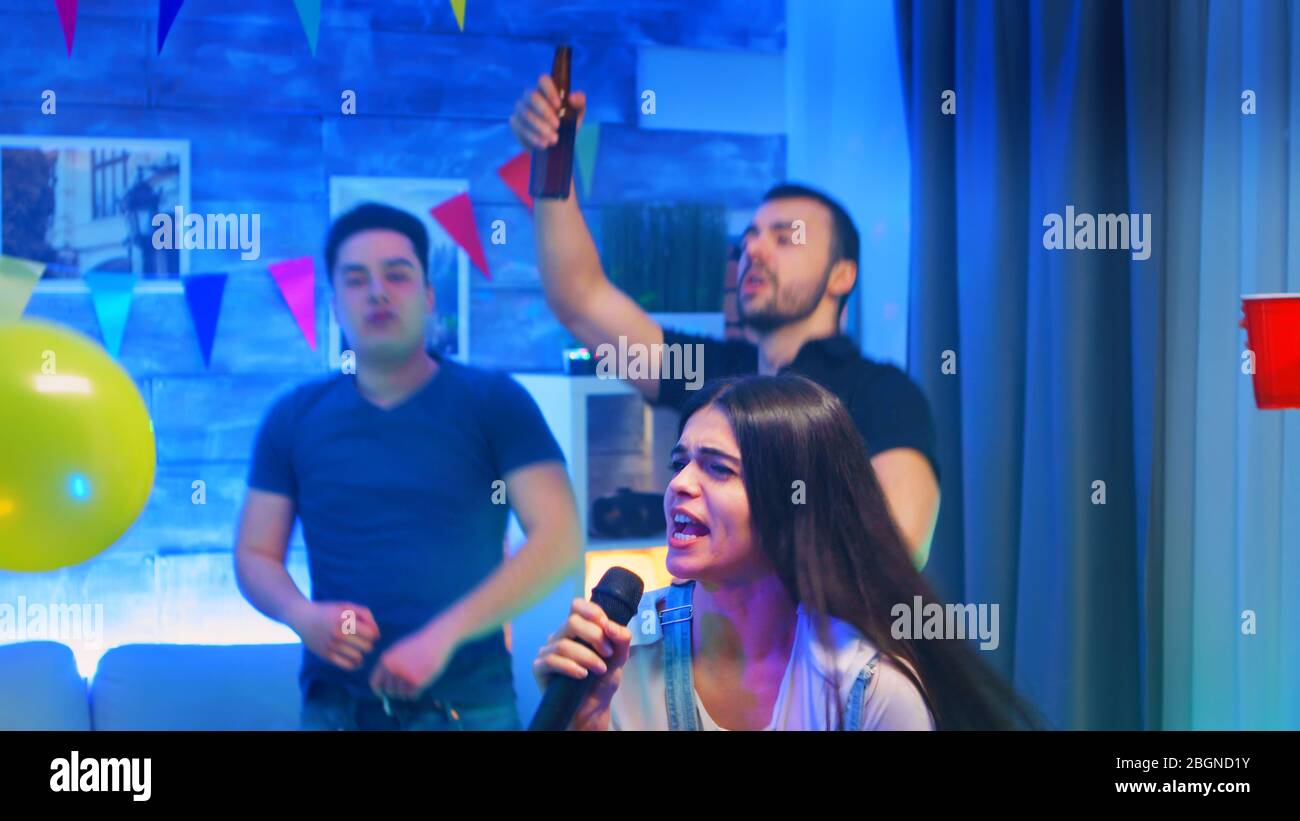 Beautiful young woman singing a song on microphone while partying with ...
