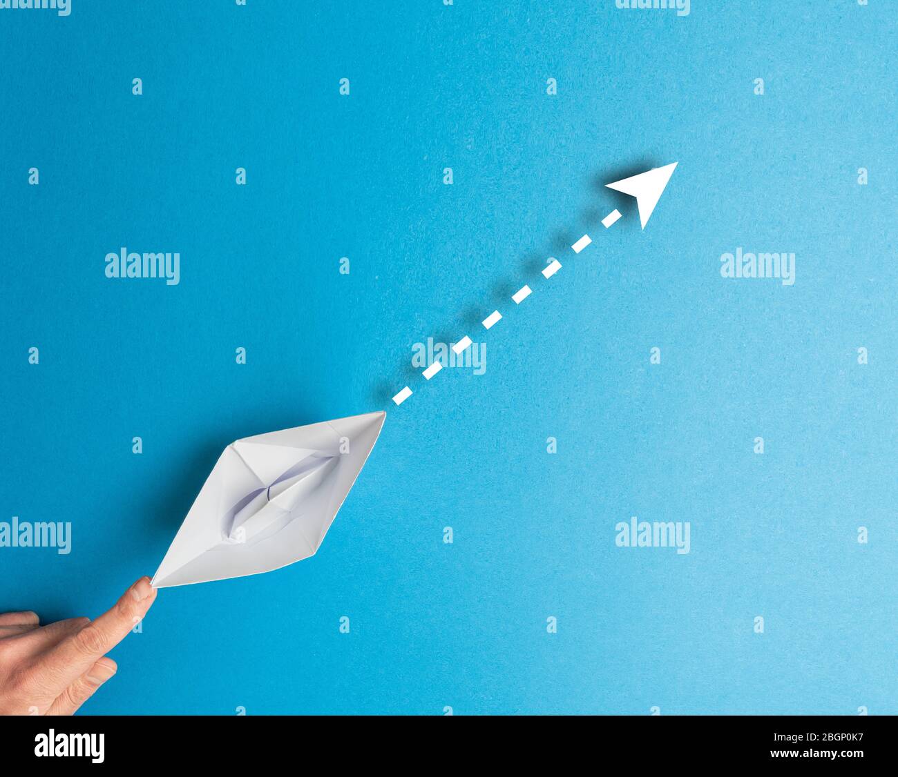 top view of hand pushing paper boat across blue background, travel and ...