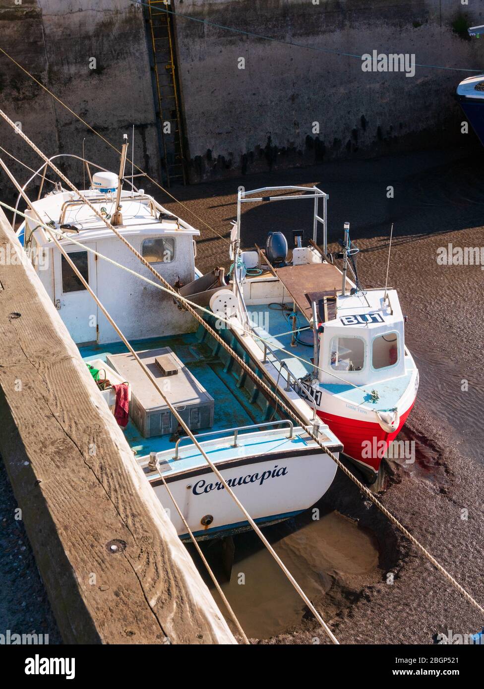 Two boats sit at low tide in the harbour in Amble, Northumberland Stock ...