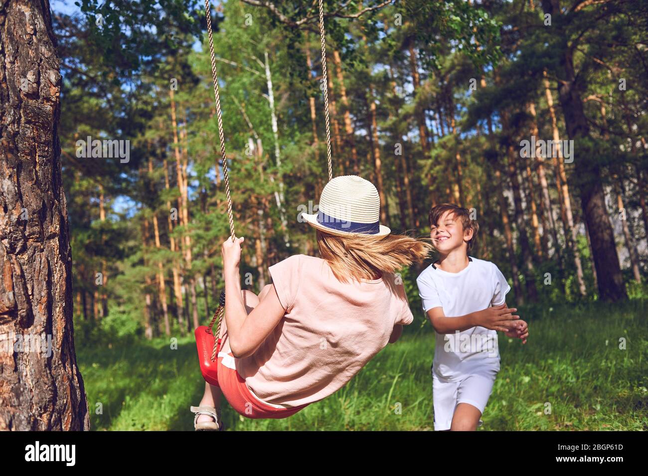 Children play and laugh in nature. A boy shakes a girl in a swing ...