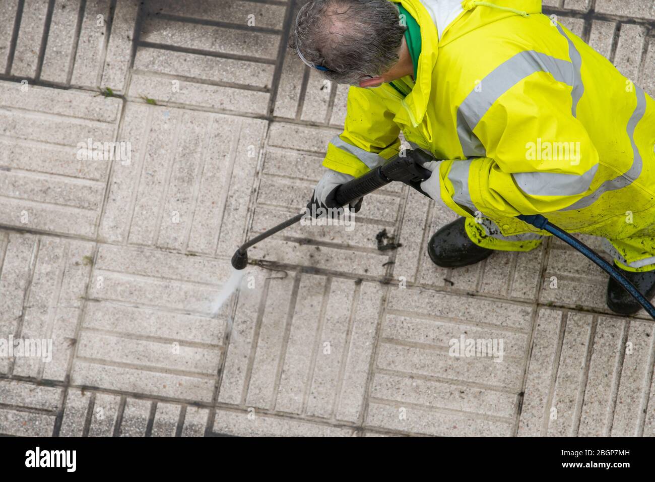 Worker cleaning the sidewalk with pressurized water. Maintenance or ...