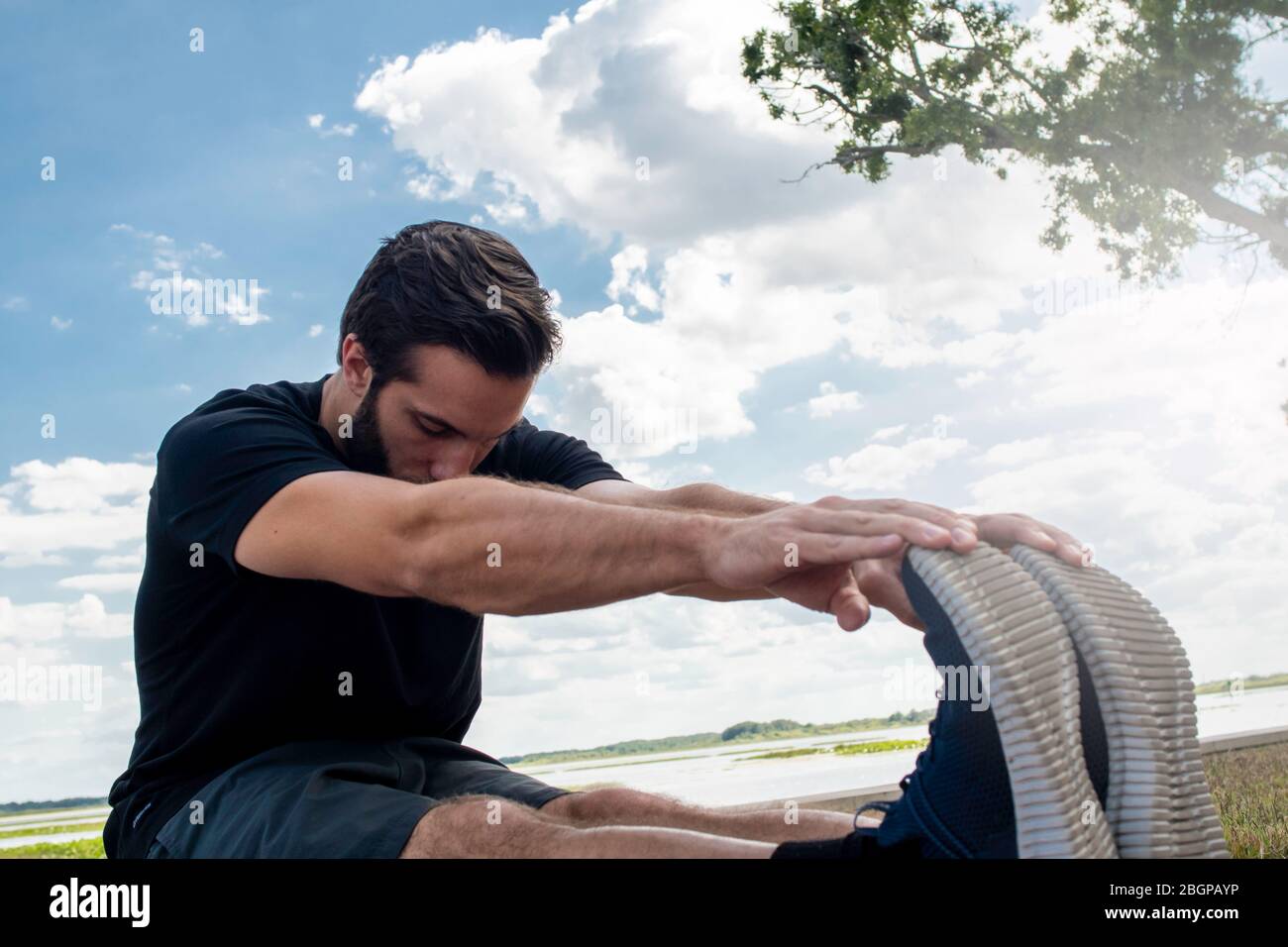 Man wearing a black shirt and dark green shorts laying forward fold ...