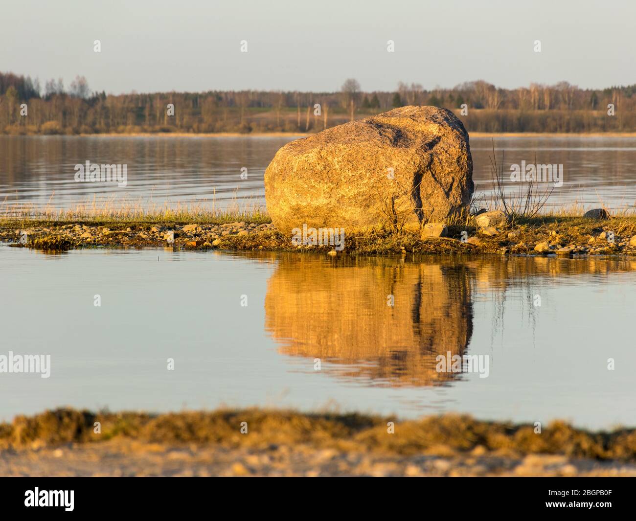 landscape with a lonely stone on the lake shore, calm lake water and ...