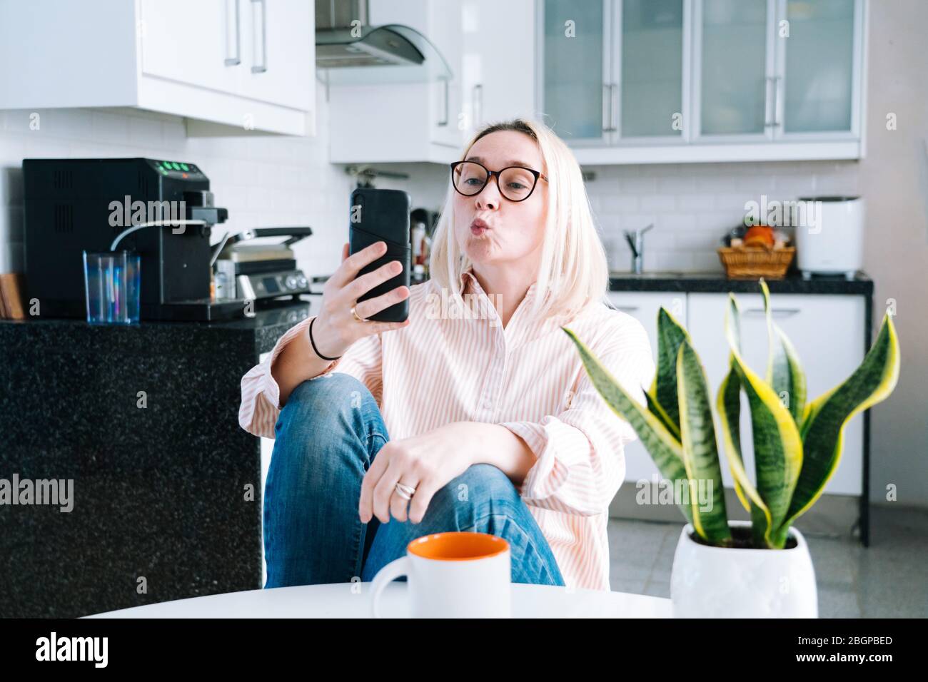 Happy girl sitting at home kitchen and holding videocall. Young woman using smartphone for video ...