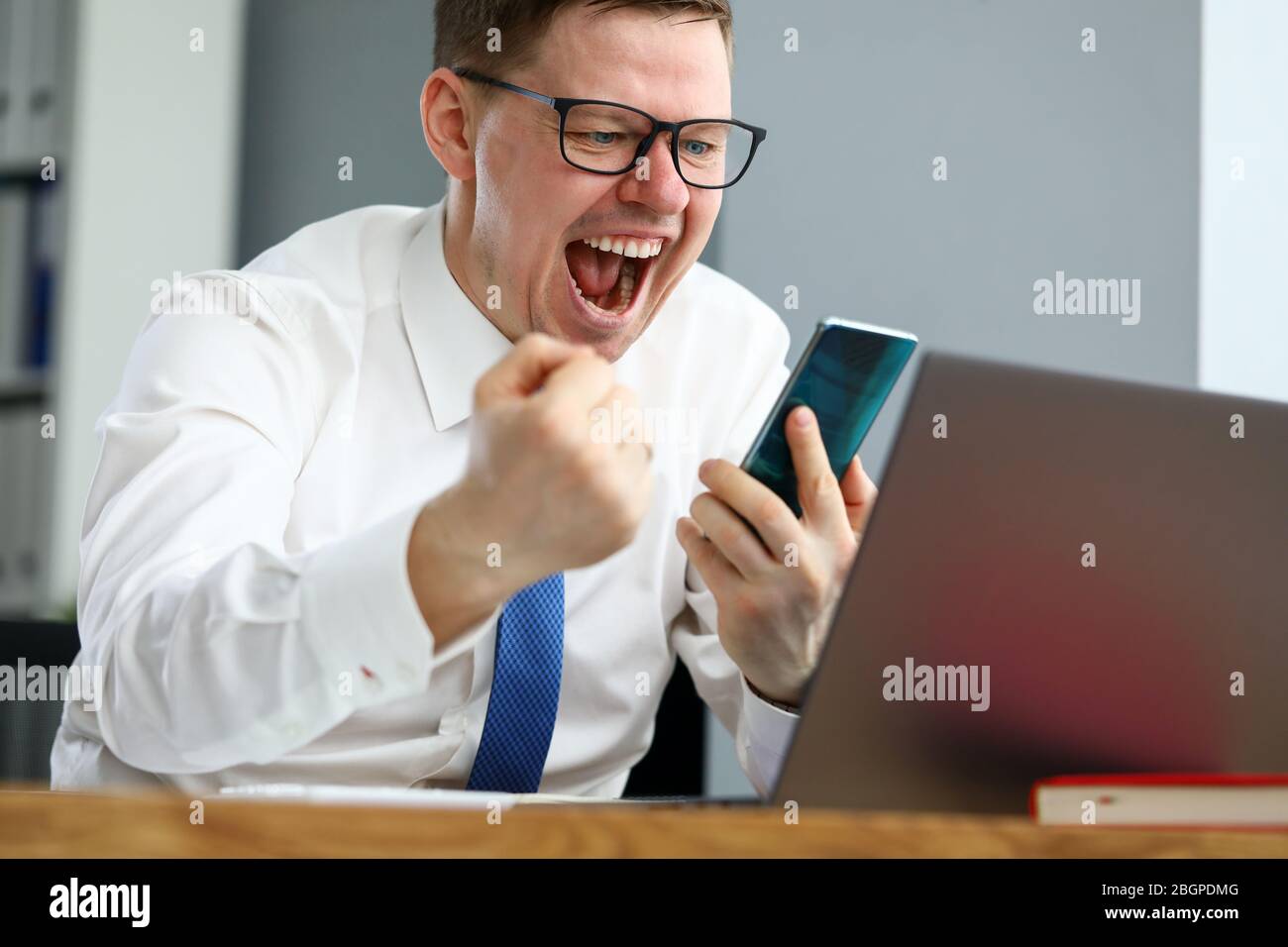 Male manager screaming and articulating while looking at smartphone ...