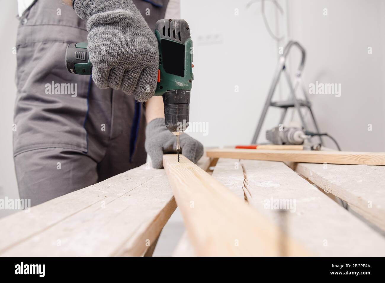 Worker man carpenter screws metal into wooden board with electric ...