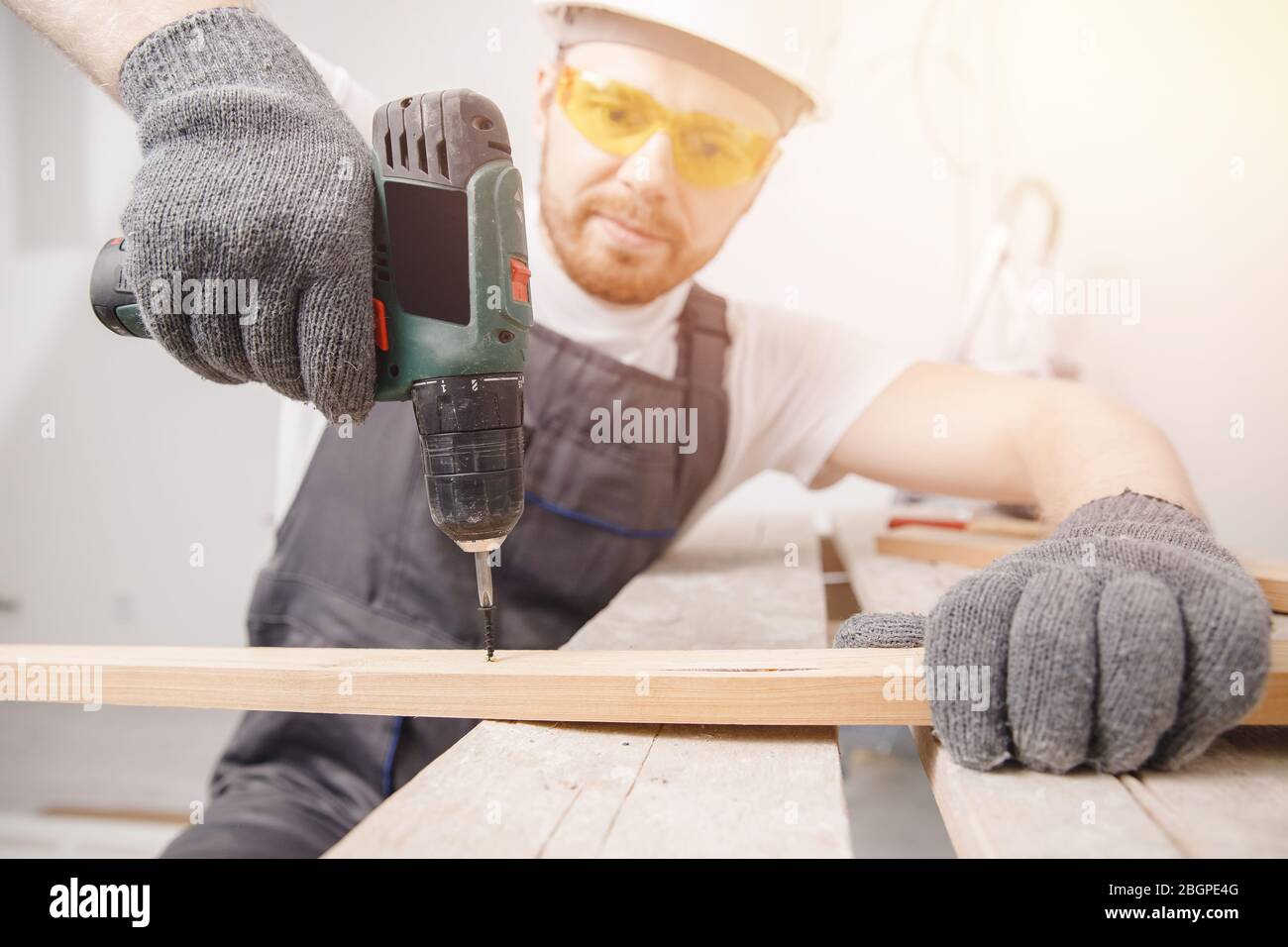 Male carpenter screws into wooden board with electric screwdriver Stock ...