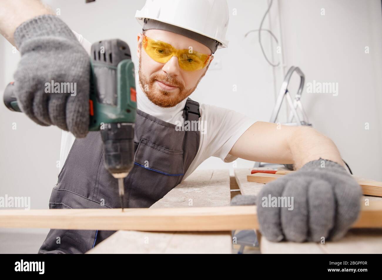 Worker man carpenter screws metal into wooden board with electric ...