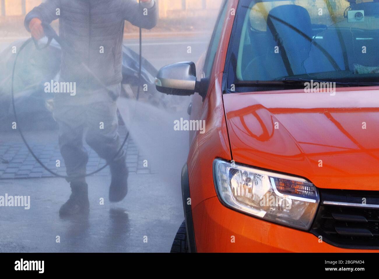 Man washes his orange car at car wash in outdoors. Cleaning with with a ...