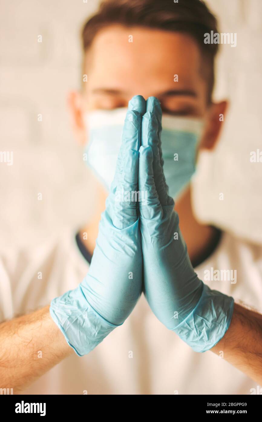 Young man prayer in protective gloves and medical face mask in church ...