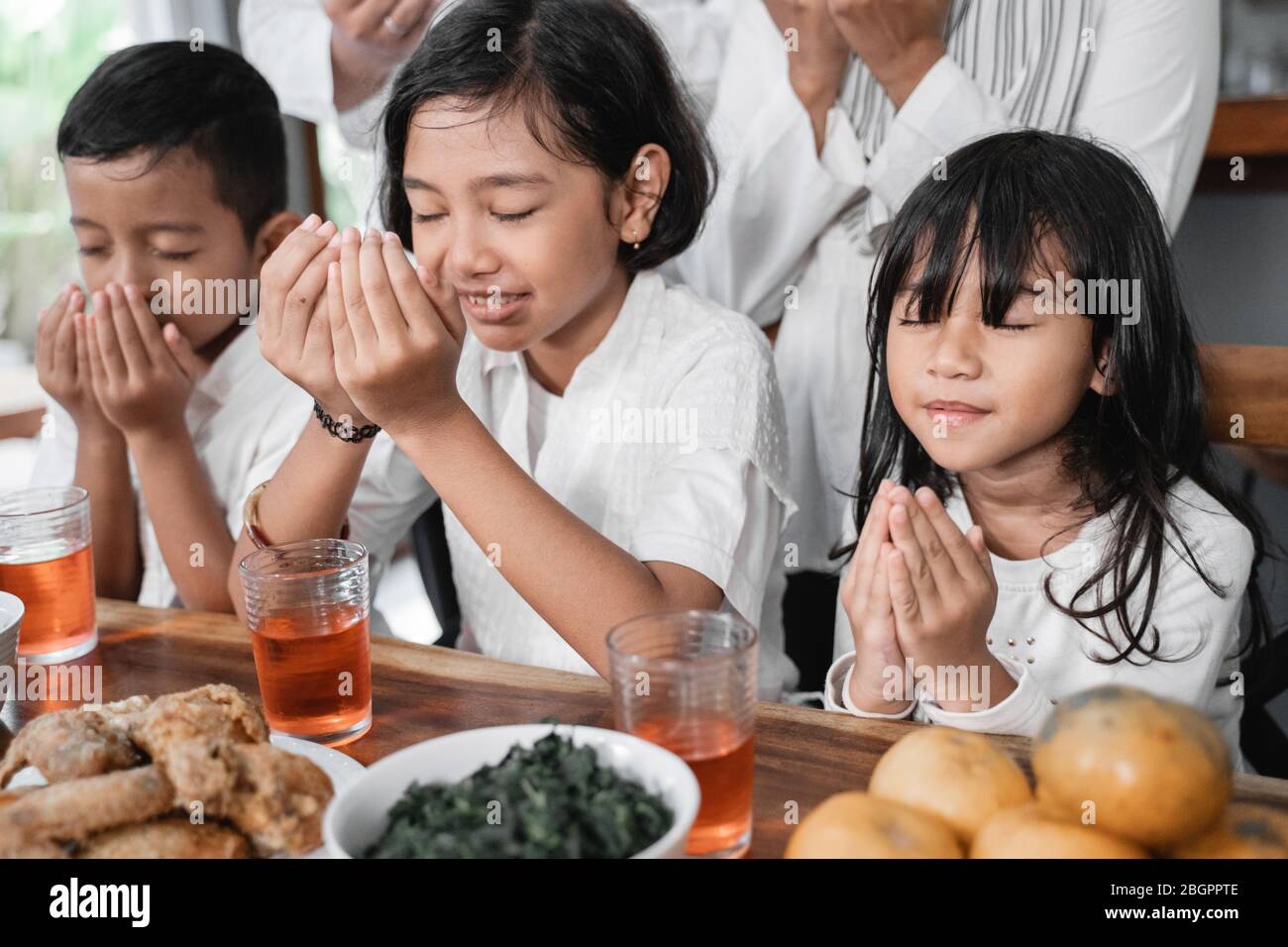 muslim family praying before eating their food. breaking the fast or ...