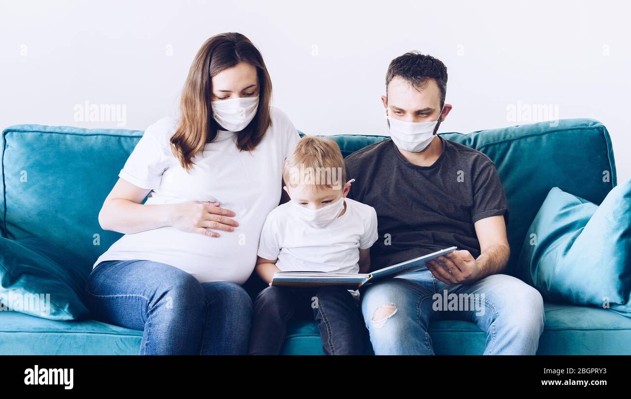 Young modern quarantined coronavirus family in medical masks reading ...