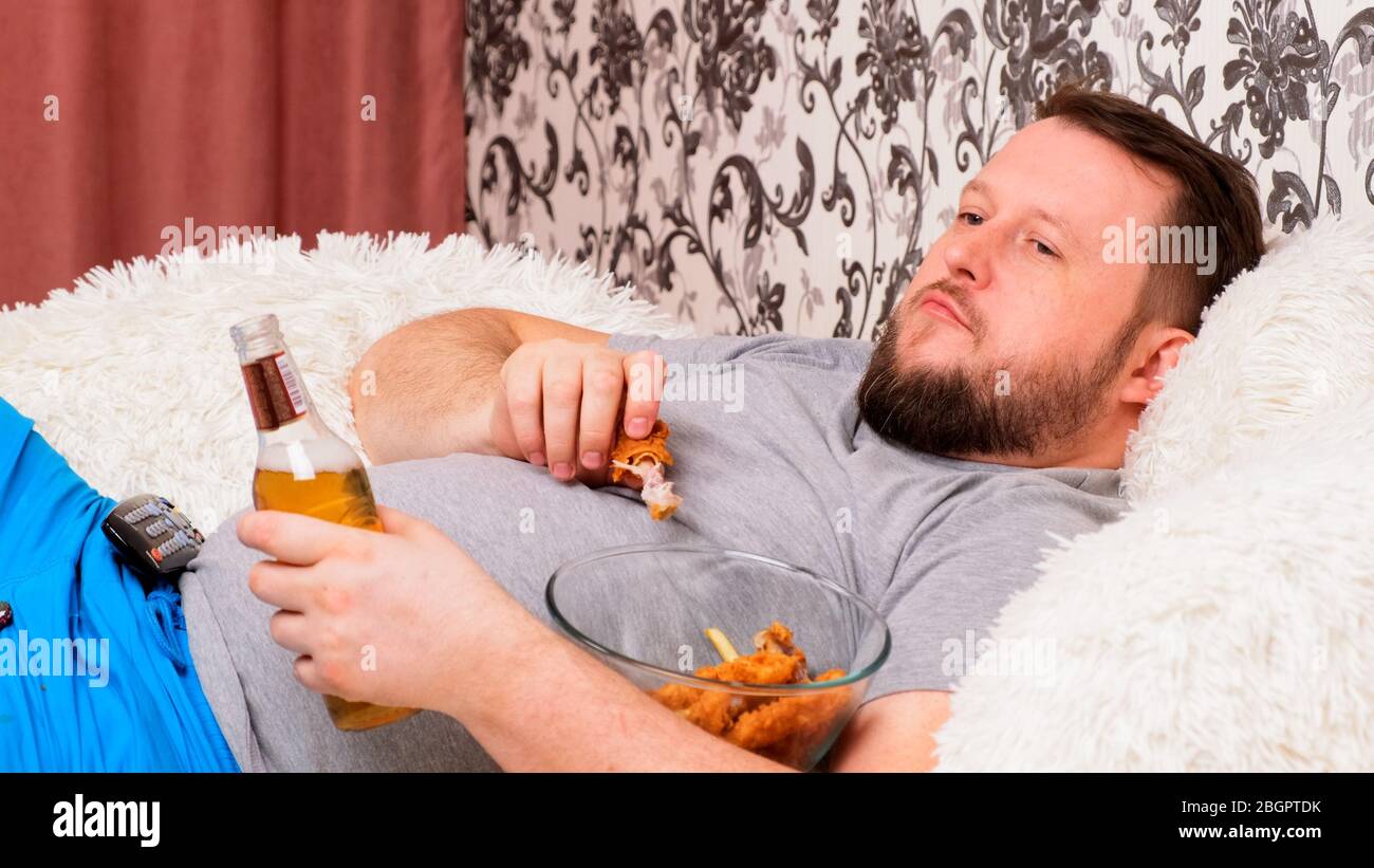 bearded Fat man with a big belly lies on the sofa with fast food ...