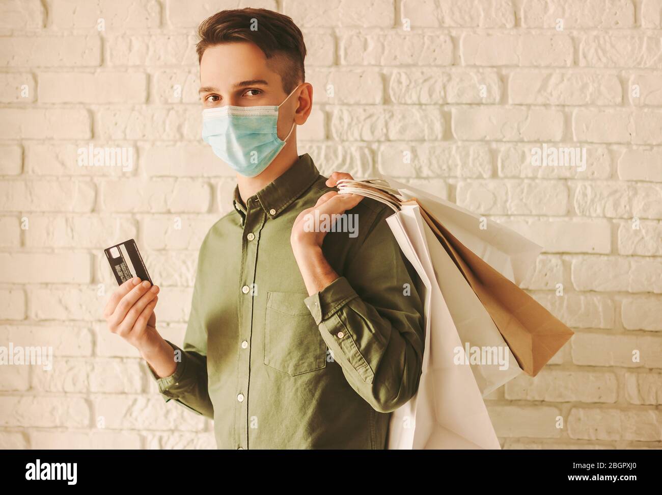 Young man in medical face mask holding credit card and shopping bags in ...