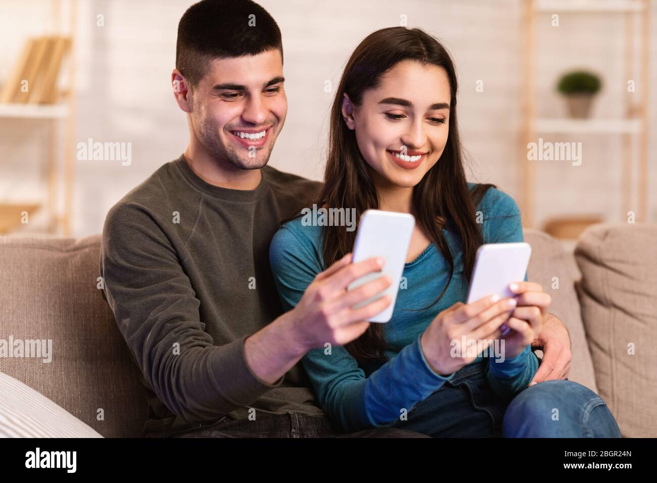 Couple using cell phones sitting on sofa Stock Photo - Alamy