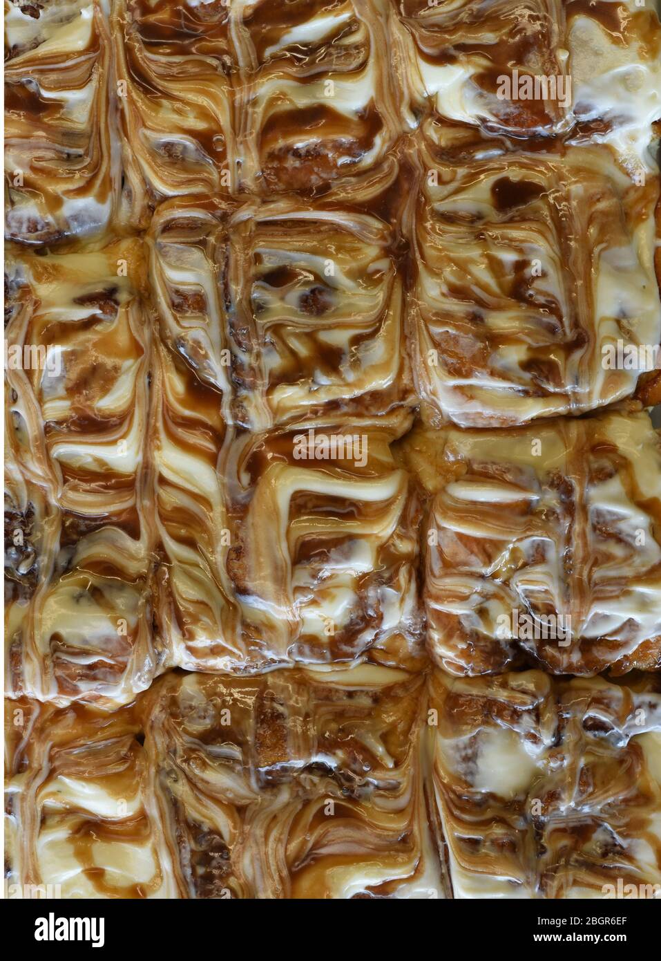 An overhead view of a tray of cinnamon buns covered in cream cheese and ...