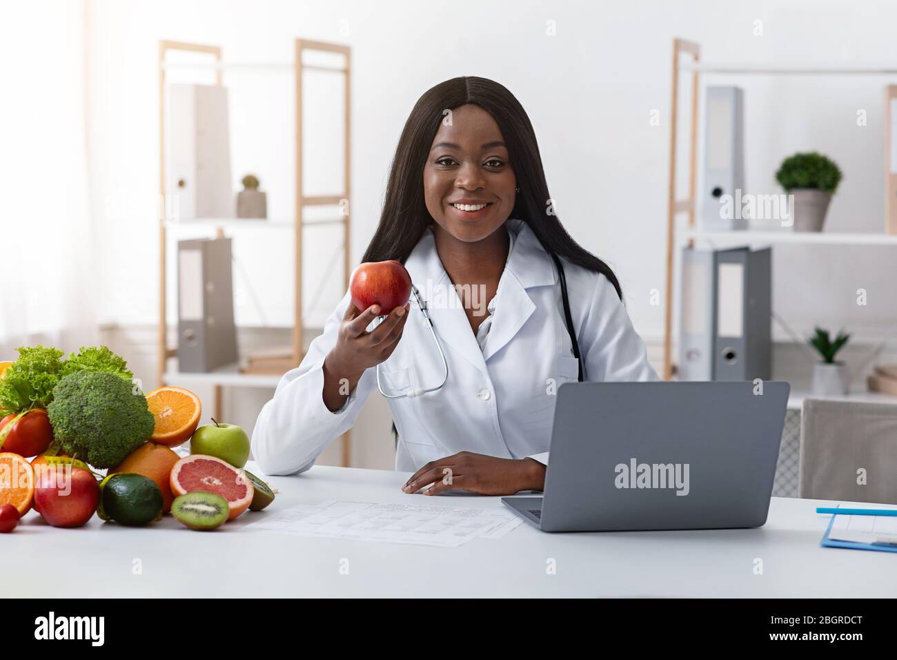 Pretty smiling black doctor recommending eating fresh fruits Stock ...