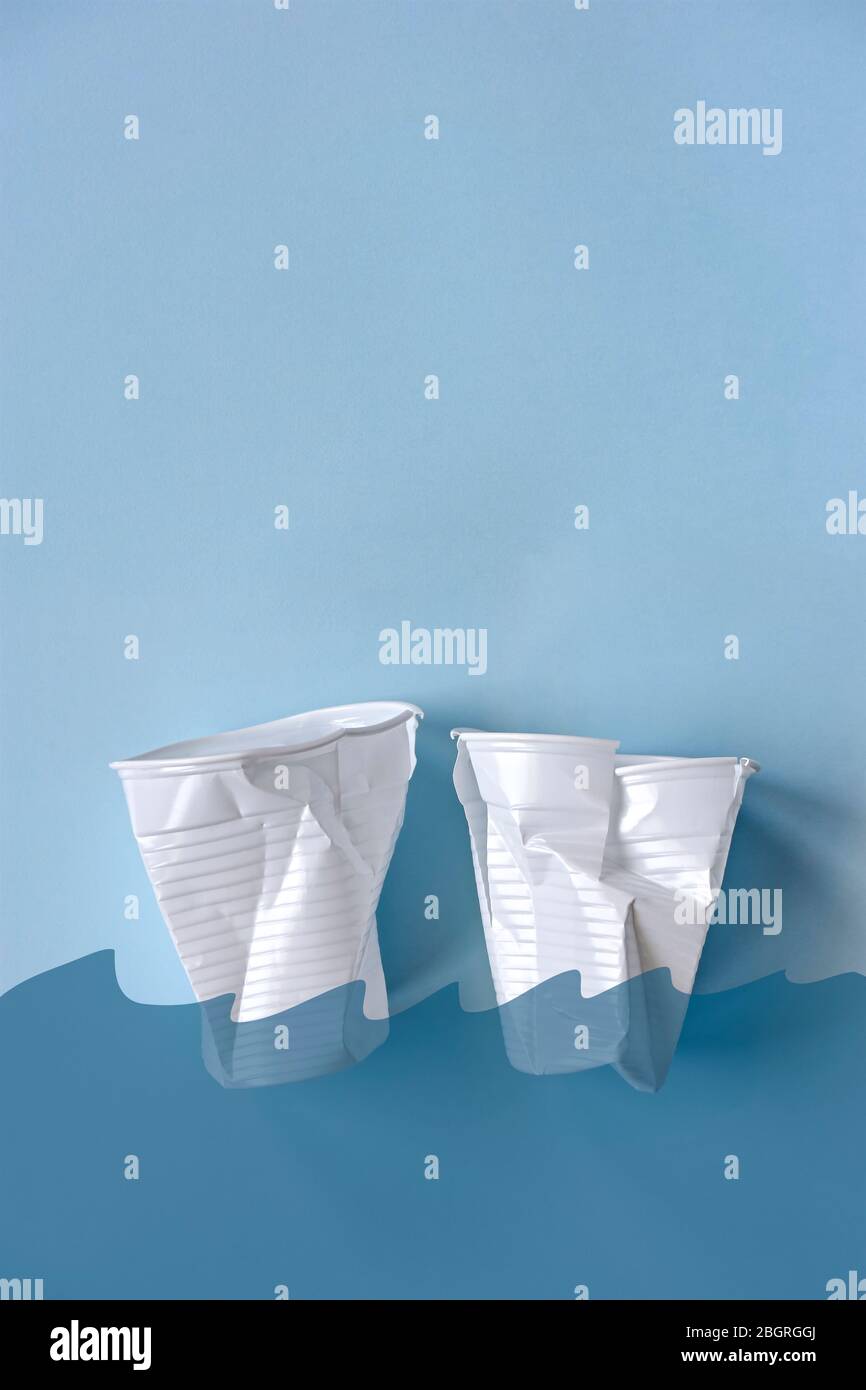 Two smashed white plastic coffee cups on a light blue background with ...