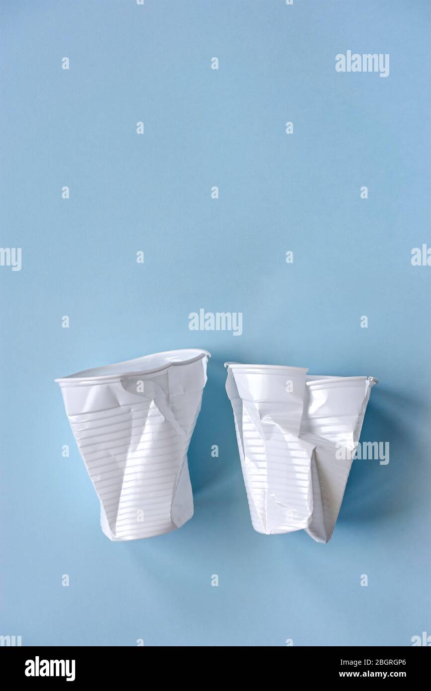 Two smashed white plastic coffee cups on a light blue background with ...