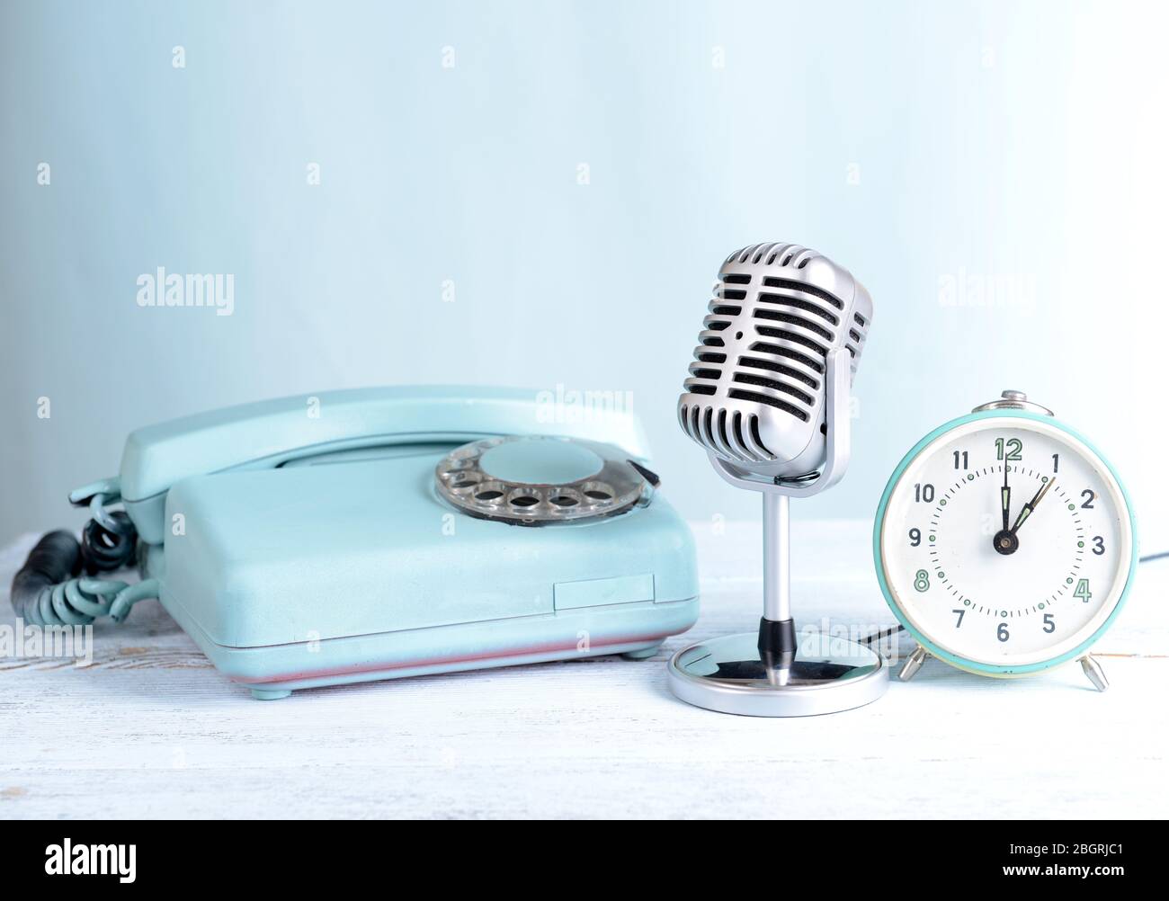 Vintage microphone,phone and alarm clock on table on light blue ...